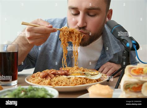 Food Blogger Eating In Front Of Microphone At Table Against Light