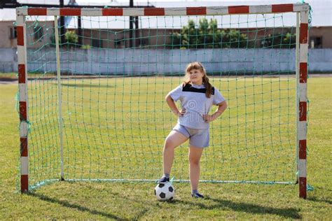 Chubby Girl In Sportswear Stands In Football Gate And Presses Ball With