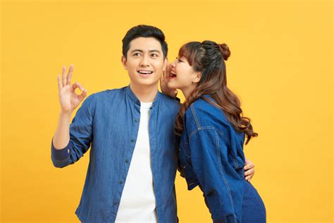 젊은 부부 두 친구 남자 여자 노란색 오렌지 벽 배경에 고립 된 포즈 사람 라이프 스타일 개념입니다 복사 공간을 모의합니다 손 뒤에 속삭이는 비밀 남자에 대한 스톡 사진 및