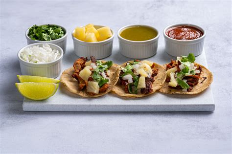 돼지 고기 토르티야 파인애플 실란트로 양파 녹색 소스 레드 소스 레몬으로 준비 타코 알 목사라는 전통적인 멕시코 길거리 음식 흰색 텍스처 배경에 길거리 타코에 대한 스톡