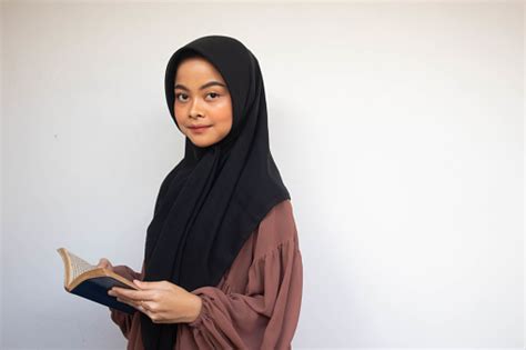 젊은 아시아 무슬림 여성이 히잡 머리 스카프를 입고 웃고 흰 배경 위에 꾸란을 들고 들고 있습니다 경전에 대한 스톡 사진 및 기타 이미지 Istock