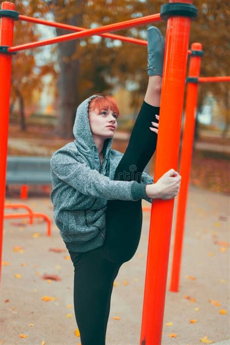 Young Hooded Gymnast Woman Warming Up At Playground Pillars And Doing