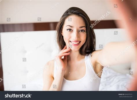 Стоковая фотография 654377212 Красивая девушка делает селфи в постели