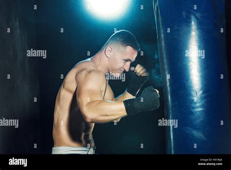Male Athlete Boxer Punching A Punching Bag With Dramatic Edgy Lighting