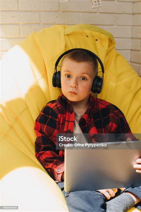 검은색 헤드폰을 쓴 학령기 소년이 손에 태블릿을 들고 노란색 콩 주머니에 앉아 있습니다 어린이 및 가제트 8 9 살에 대한 스톡 사진 및 기타 이미지 Istock