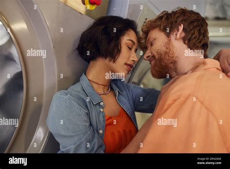 Young Multiethnic Romantic Couple Kissing Near Washing Machine In