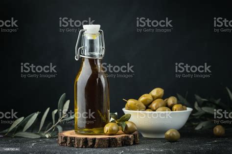 올리브 오일이 든 병 옆에 흰색 그릇에 담긴 녹색 올리브와 검은색 배경에 나뭇잎 냉간 압착 오일 한 병 전통적인 그리스와