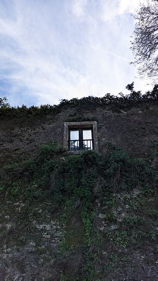 하늘과 구름을 볼 수있는 파괴 된 집의 오래된 벽에있는 창문은 이끼와 다양한 식물로 무성하게 자란 벽 하나만 남았습니다 건설