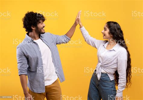 일반적인 성공 젊은 흥분 인도 부부는 하이파이브를주고 박수를 치고 노란색 배경을 통해 서로 인사 하이 파이브에 대한 스톡 사진