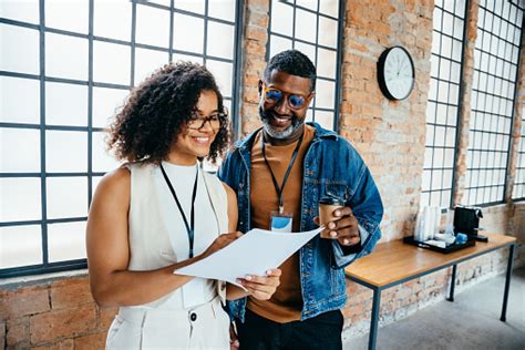인더스트리얼 스타일의 사무실 환경에서 미소와 커피를 마시며 프로젝트를 논의하는 행복한 동료들 2명에 대한 스톡 사진 및 기타