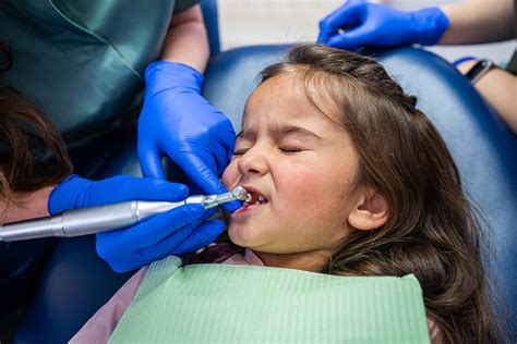 특별한 옷을 입은 젊은 자격을 갖춘 치과 의사가 치과 의자에 있는 어린 소녀의 치아를 치료합니다 3 명에 대한 스톡 사진 및 기타 이미지 Istock