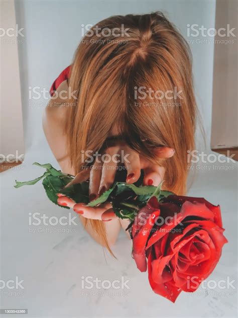 빨간 네글리지에 매력적인 외모를 가진 젊은 갈색 머리의 여성이 손에 빨간 장미 꽃이 달린 종이 캔버스에 포즈를 취하고 있습니다