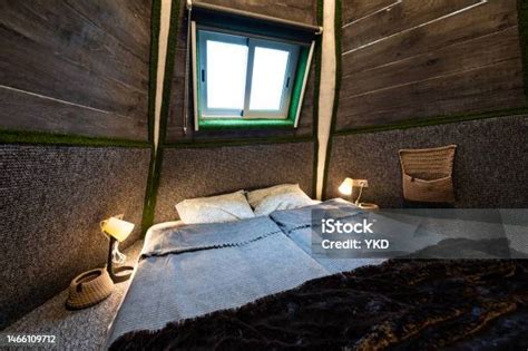 나무 오두막의 침실에 있는 카펫 바닥에 있는 더블 침대 내부에서 피라미드 모양의 방갈로 작은 방 각진 벽 창문 조명 만든 침대 나무 오두막의 수제 인테리어 가구에 대한 스톡
