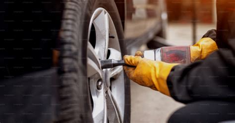 주황색 장갑을 낀 숙련 된 열심히 일하는 정비사가 전기 렌치를 사용하여 자동차 바퀴의 나사를 조이고 있습니다 사진 Unsplash의 바퀴 이미지