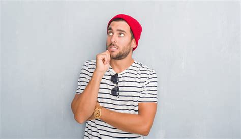 회색 그런 지 위에 잘생긴 젊은 Hipster 남자 턱 질문 잠겨있는 표현에 대 한 생각에 손으로 해군 착용 T셔츠와 양모 모자