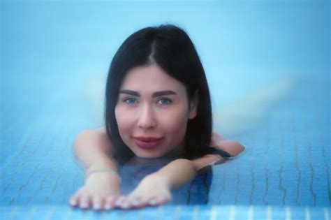 美しいブルネットの女性は、温泉リゾートのスパのプールでミネラルウォーターに横たわってリラックスします。カメラを見ているモデル。目にソフトセレクティブフォーカス。 プレミアム写真