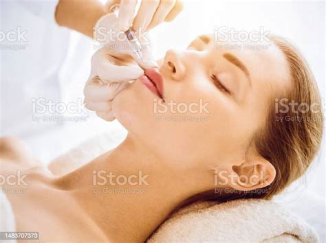 햇볕이 잘 드는 의료 센터에서 눈을 감고 미용 주사를 받는 아름다운 여성 미용사 의사는 주사기로 여성의 얼굴에 미용 시술을 하고