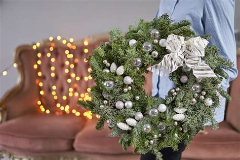 크리스마스 분위기입니다 여자의 손에 신선한 가문비 나무의 아름다운 축제 화환 Xmas 나무입니다 배경에 화환의 보케가 켜지다
