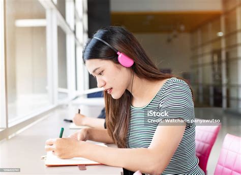 그녀의 머리에 헤드폰을 착용 하는 젊은 십 대 책에 쓰기 회의실에서 숙제를 하 고 주위 흐리게 빛 교육에 대한 스톡 사진 및 기타 이미지 Istock