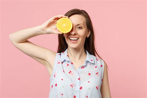 분홍색 파스텔 배경에 고립 된 신선한 잘 익은 오렌지 과일의 Halfs와 눈을 덮고 있는 여름 옷을 들고 있는 젊은 여자를 웃는 사람들은 생생한 라이프 스타일 휴식 휴가