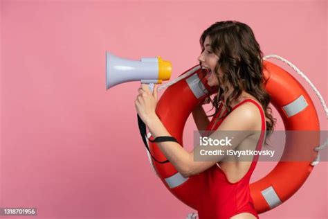 분홍색 배경에 매력적인 젊은 인명 구조원의 측면 보기는 라우드 스피커로 이야기 그의 어깨에 구명 부표와 수영복을 입은 소녀 젊은