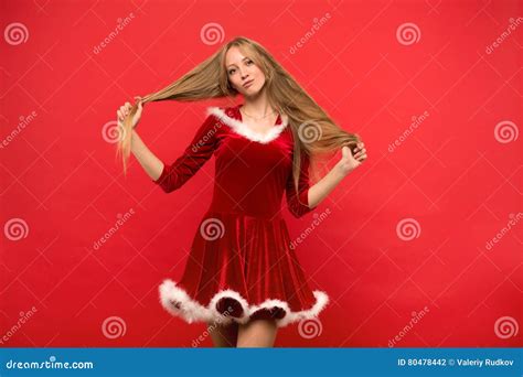 Красивая молодая женщина в костюме Санты играя при стренга ее длинных шелковистых волос смотря