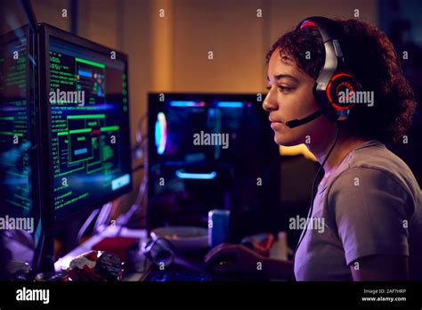 Female Teenage Hacker Sitting In Front Of Computer Screens Bypassing Cyber Security Stock Photo