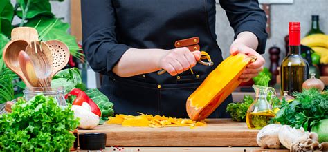 주부는 야채 필러로 호박 껍질을 벗깁니다 나무 테이블 주방용품 야채 허브 요리 재료가 있는 아늑한 주방 건강한 비건 채식 요리 조리법 음식 블로깅 가정 주방에 대한 스톡