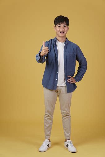노란 배경에 고립 된 표정을 승인 하는 제스처와 함께 캐주얼 옷을 입고 웃는 긍정적 인 젊은 아시아 남자의 초상화 20 24세에