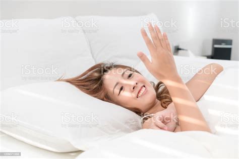 매력적인 미소와 아름다운 아시아 여성의 초상화는 흰색 침대 방 현대 아파트에서 신선한 부드러운 침구 린넨 매트리스를 즐길 수