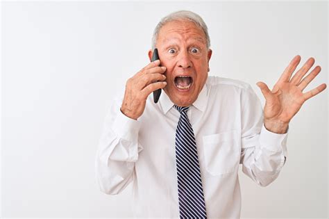 고립 된 흰색 배경을 통해 스마트 폰에 말하는 선임 회색 머리 사업가는 매우 행복하고 흥분 큰 미소와 손을 들고 비명을 지르는