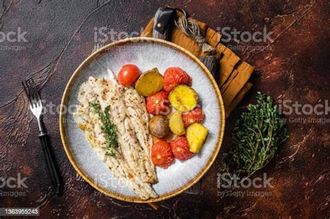 구운 폴락 생선 필레에 토마토와 감자를 곁들인 접시에 구운 어두운 배경 위쪽 보기 메를루사에 대한 스톡 사진 및 기타 이미지