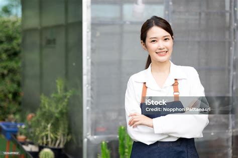팔이 교차 서 집 공장에서 일하는 유니폼을 입은 젊은 귀여운 아시아 여성 온실에서 나무를 돌보는 아시아 여성 홈 컨셉에서 소규모