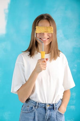 파란 배경에 고립 된 벽화에 페인트 롤러를 들고 캐주얼 옷을 입고 젊은 미소 아름다운 여자 악기 액세서리 리노베이션 아파트 룸을위한 도구 수리 홈 컨셉 25 29세에 대한