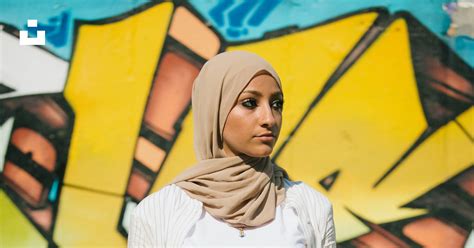 흰색 긴 소매 셔츠와 파란색 데님 반바지를 입은 여자가 노란색과 검은색 벽 옆에 서 있다 사진 Unsplash의 무료 미국 이미지