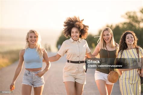 일몰에 자연의 도로에서 행복하고 미소 걷고 있는 네 명의 젊은 다인종 여성 젊은 여자에 대한 스톡 사진 및 기타 이미지 젊은