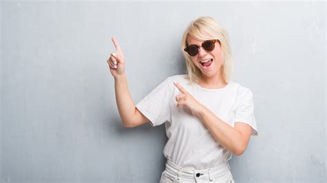 웃 고 옆에 두 손과 손가락으로 가리키는 카메라 보고 선글라스를 착용 하는 그런 지 회색 벽에 성인 백인 여자 가리키기에 대한 스톡 사진 및 기타 이미지 Istock