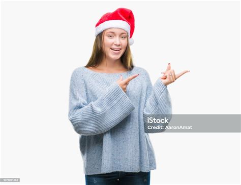 젊은 아름 다운 백인 여자 웃 고 옆에 두 손과 손가락으로 가리키는 카메라 보고 격리 된 배경 위에 크리스마스 모자를 쓰고