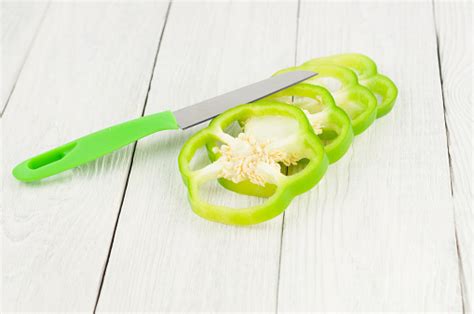 오래 된 시골 백색 나무 판자에 녹색 신선한 원료 고추와 녹색 플라스틱 손잡이 가진 금속 칼 슬라이스 0명에 대한 스톡 사진 및