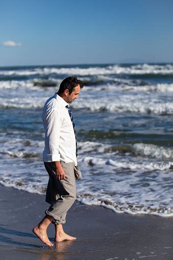 관상 느슨한 흰색 셔츠와 넥타이와 롤업 바지를 가진 중 년 기업 남자 침착 하 게 그의 손에 코트와 함께 바다를 향해 해변에서 맨발로 걷기 걷기에 대한 스톡 사진 및 기타