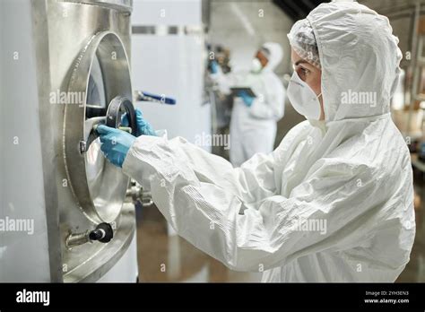 Side View Of Female Process Technician Wearing Hazmat Suit And Protective Gloves Turning Valve