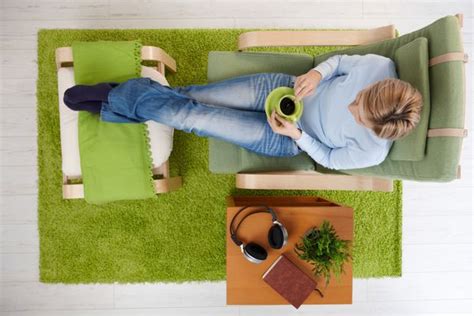 زن در حال خوردن قهوه روی صندلی راحتی با پاهای ضربدری روی تخته پا در