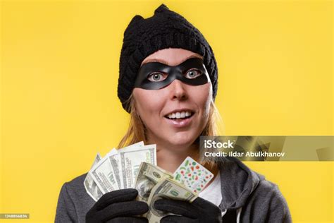 사이버 범죄 및 돈 도난 모자 장갑 가면을 쓴 한 여성이 손에 돈을 들고 꿈꾸며 위를 올려다본다 노란색 배경입니다 복사 공간 도둑질 범죄에 대한 스톡 사진 및 기타 이미지