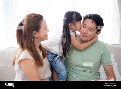 Glückliche asiatische Familie Tochter küsst Wange Vater und Mutter sitzen auf dem Sofa im