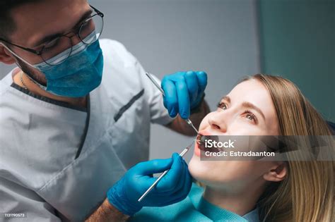 특수 도구를 사용 하 여 고객의 치아를 검사 하는 치과 의사의 클로즈업 젊은 여성은 방에서의 자에 앉아서 입을 열어 둡니다 그녀는 올려 다 봐 개성 개념에 대한 스톡 사진