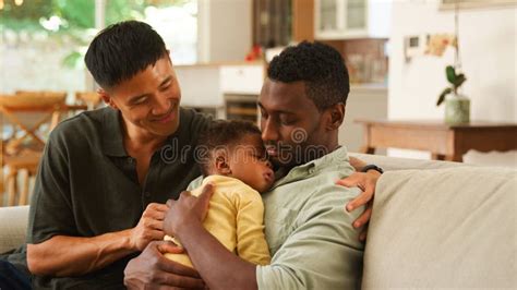 Same Sex Male Couple Bonding At Home With Infant During Daytime Stock