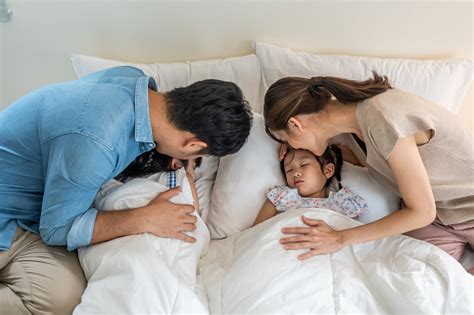 아시아의 사랑하는 부모는 집에서 침실에서 자고있는 딸을 돌봅니다 매력적인 행복한 가족 부부 어머니와 아버지는 아침에 침대에서
