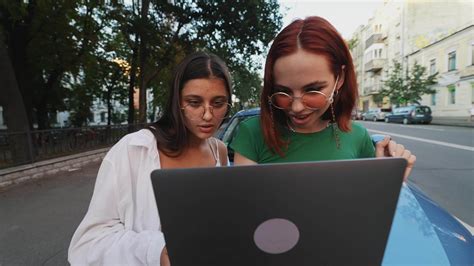 dos mujeres jóvenes miran una computadora portátil cerca de un auto