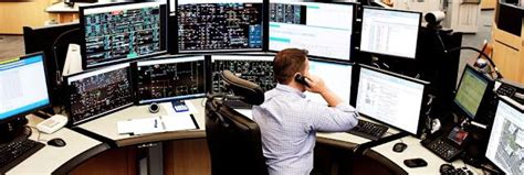 a man sitting at a desk with multiple computer screens on the wall and