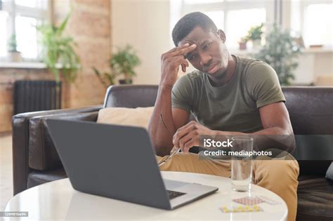 심각한 두통을 앓고 있는 안경을 들고 노트북 앞에서 책상에 앉아 있는 젊은 성인 아프리카계 미국인 남자 25 29세에 대한 스톡 사진 및 기타 이미지 Istock